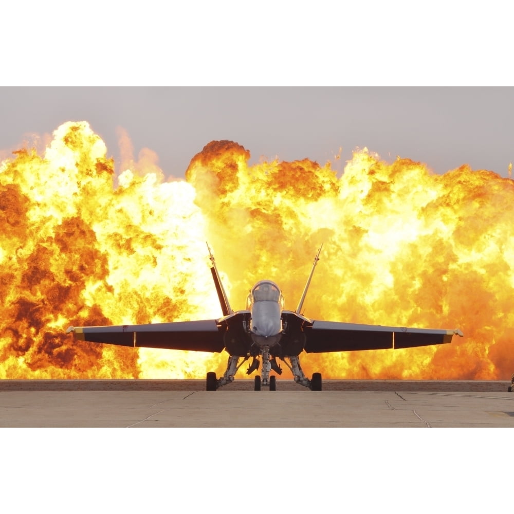 An F/A-18 Hornet sits on the flight line as a wall of fire detonates ...