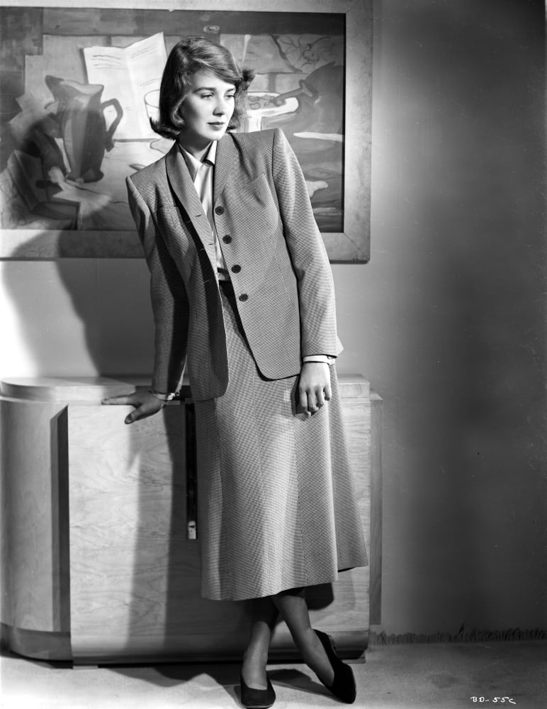 Betsy Drake Posed with Right Hand on the Table Legs Crossed in Grey ...