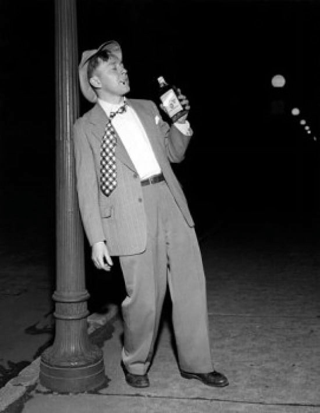Drunk mid adult man leaning against a lamppost holding a bottle of ...