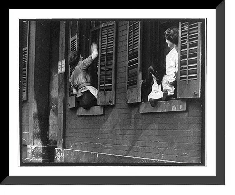 Historic Framed Print, [Woman sitting on ledge washing tenement windows ...