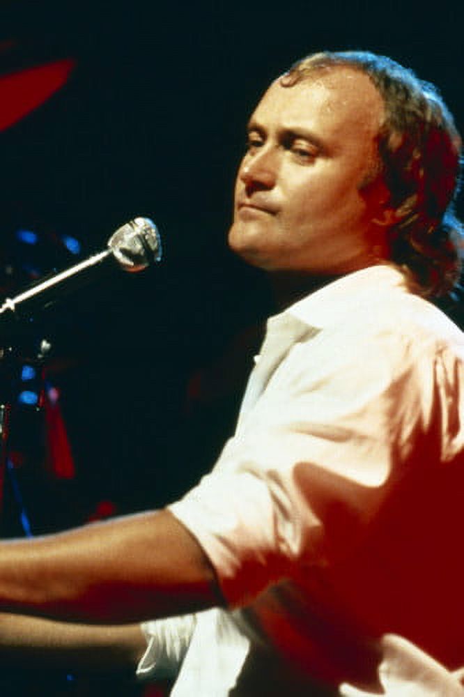 Phil Collins in concert seated at piano in shirtsleeves playing piano ...