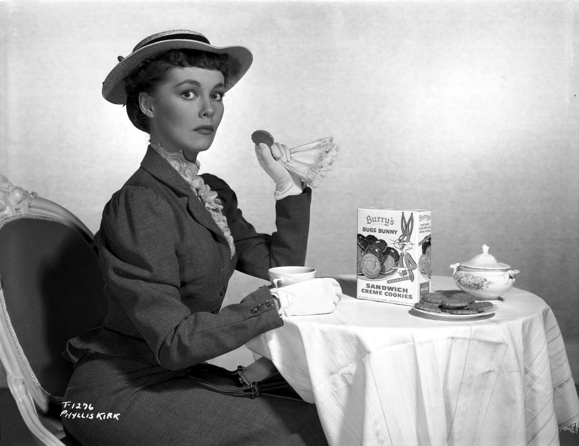 Phyllis Kirk Seated while Holding Cookie in Black Formal Dress with Hat ...