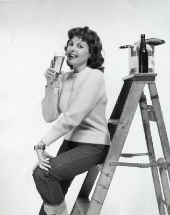 Portrait of a young woman sitting on a step ladder and drinking beer ...