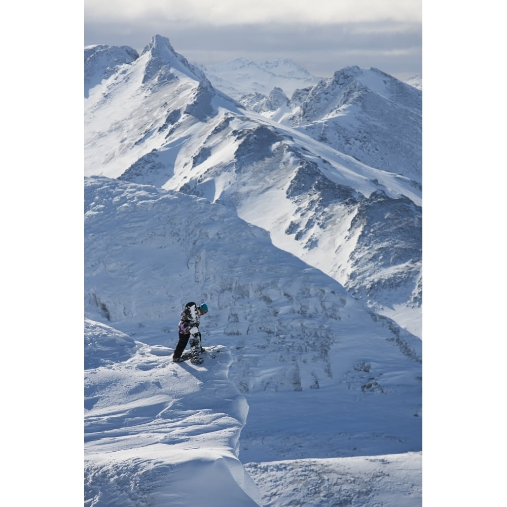 Professional snowboarder looking over the ledge at extreme terrain ...