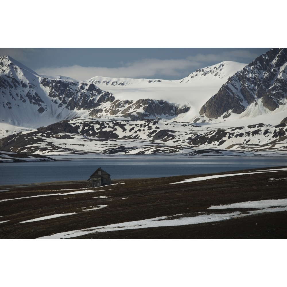 Small wooden cabin on the shore of the Arctic Ocean and snow covered ...
