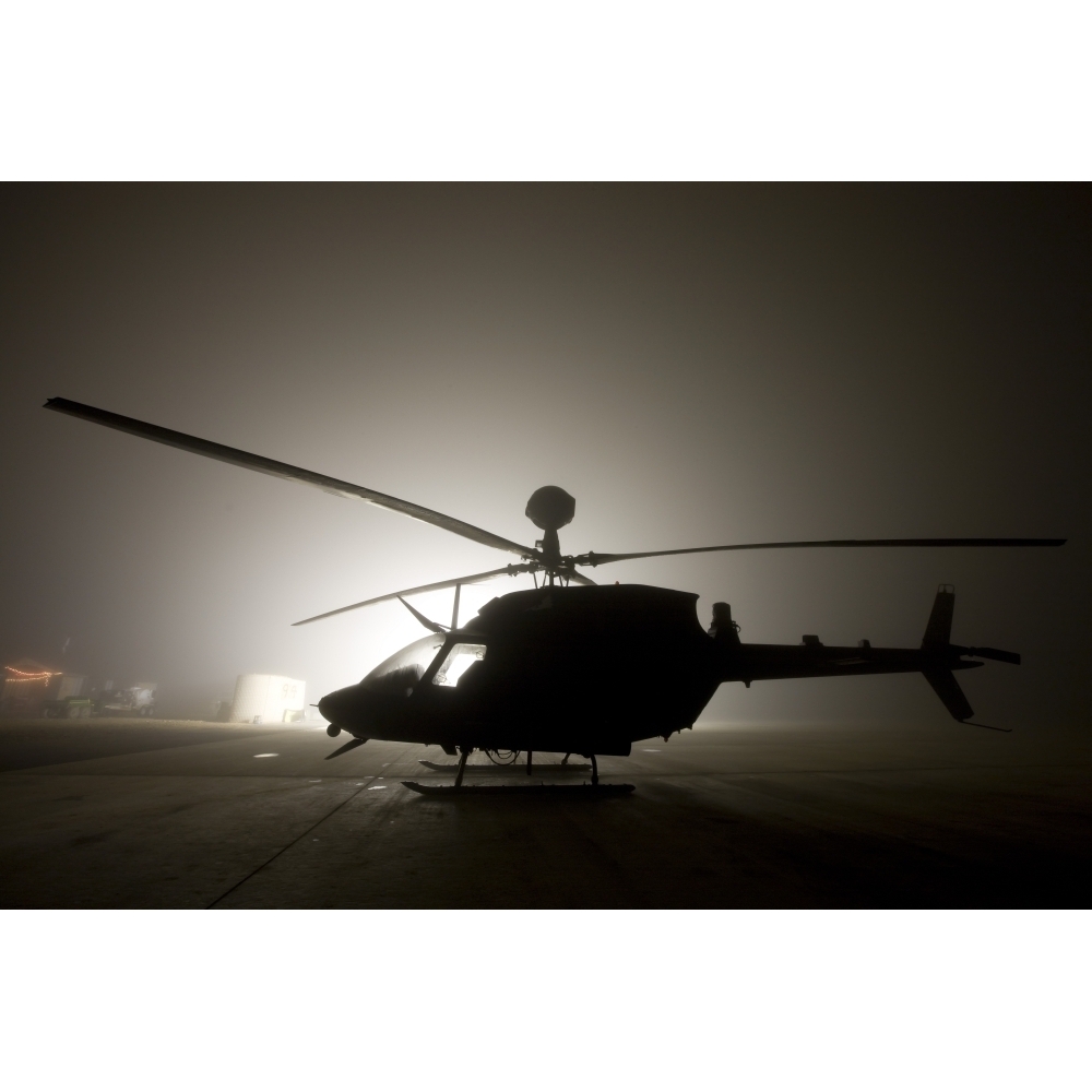 The illumination from the bright light silhouettes a OH-58D Kiowa ...