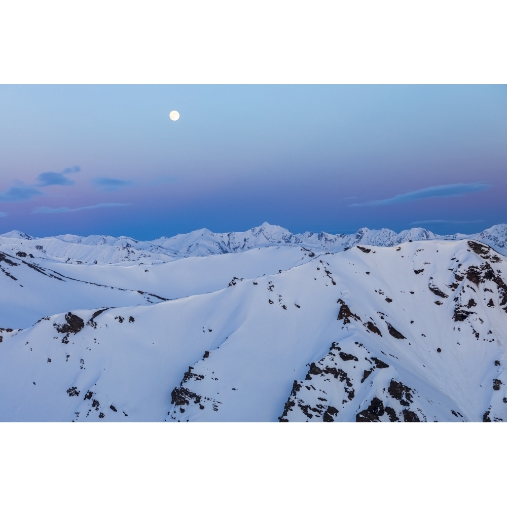 The moon rises over snowy mountain ridges after sunset in the Alaska ...