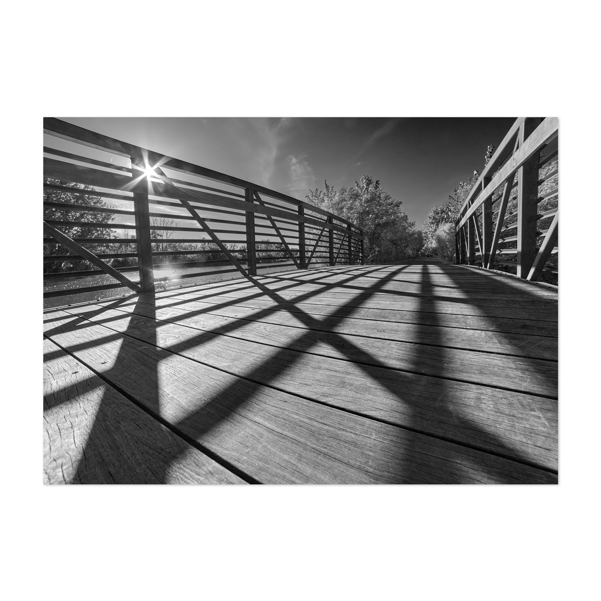 The late day sun throws long shadows on this footbridge next to a small ...